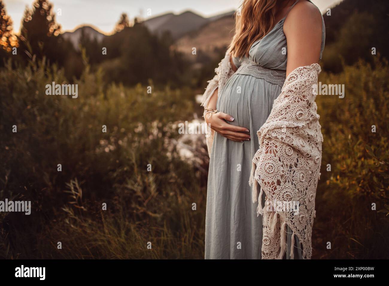 Expecting mother cradling belly, light blue dress and soft lace blanket ...