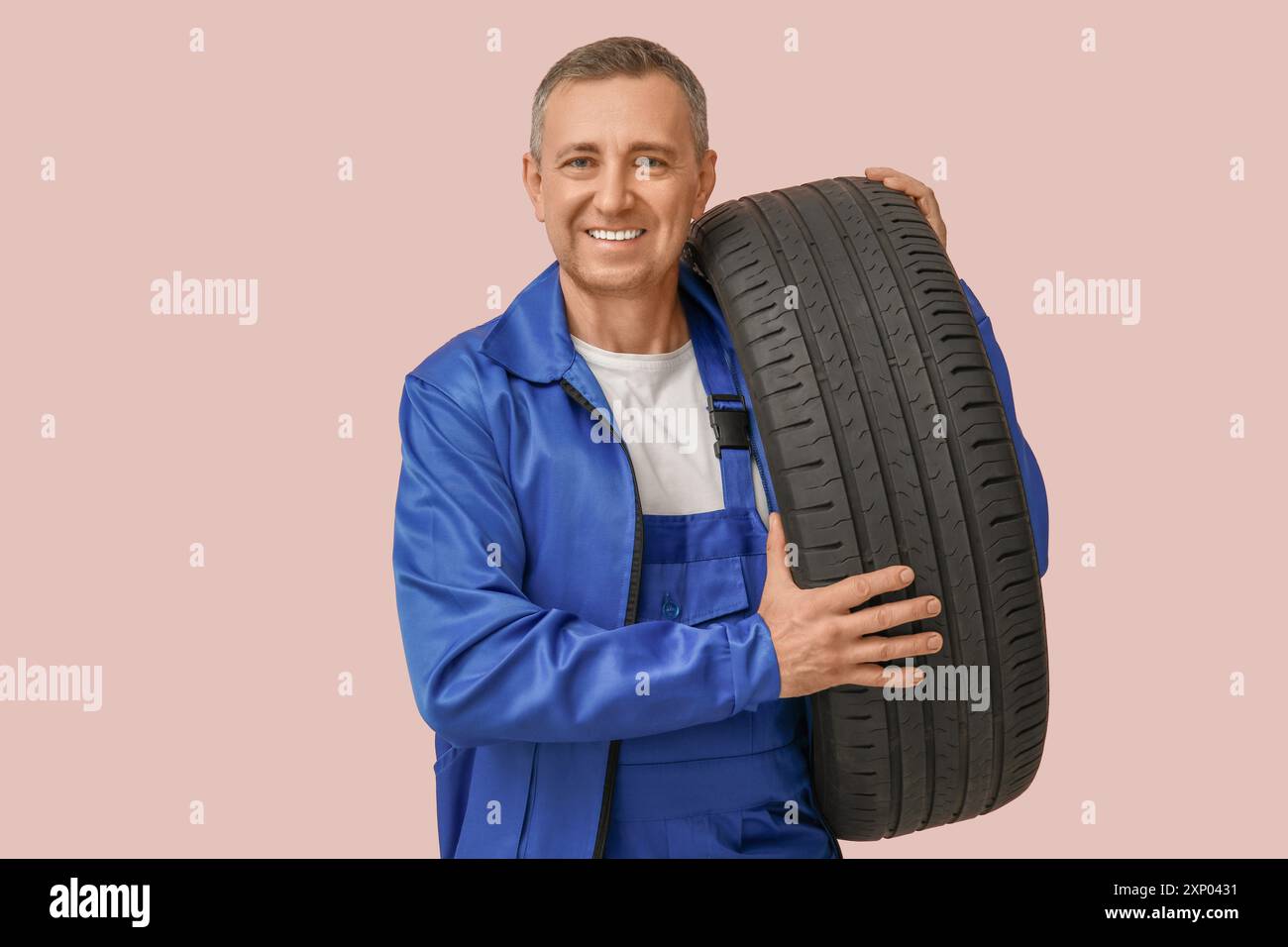 Portrait of male auto mechanic with tire on pink background Stock Photo ...
