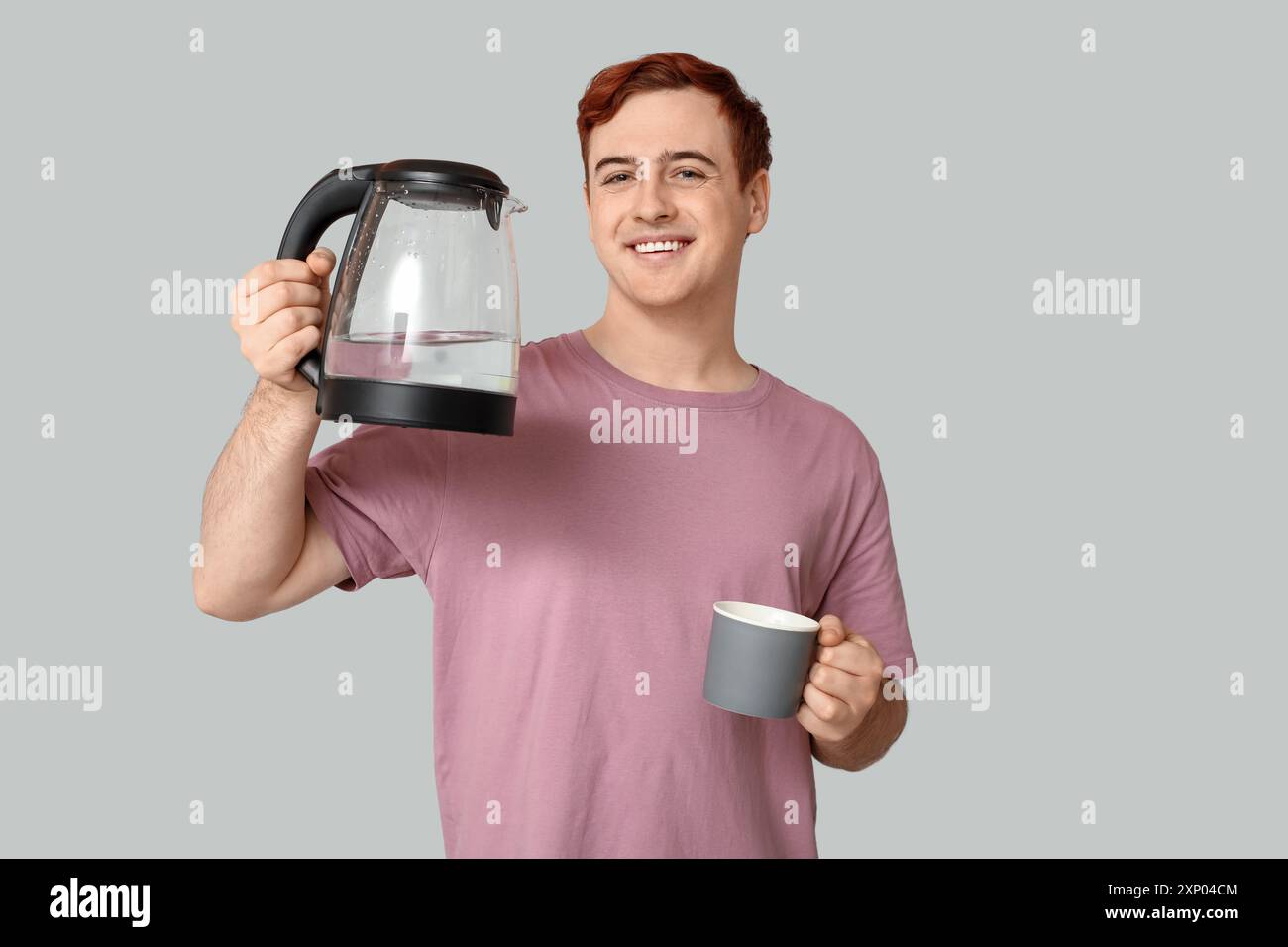 Shocked young man with modern electric kettle and mug on grey ...