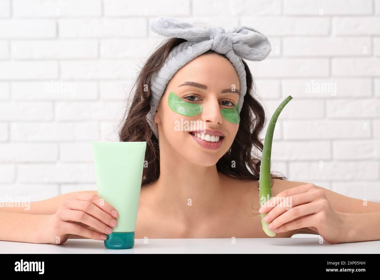 Beautiful young woman with aloe vera leaves and tube of cosmetic ...