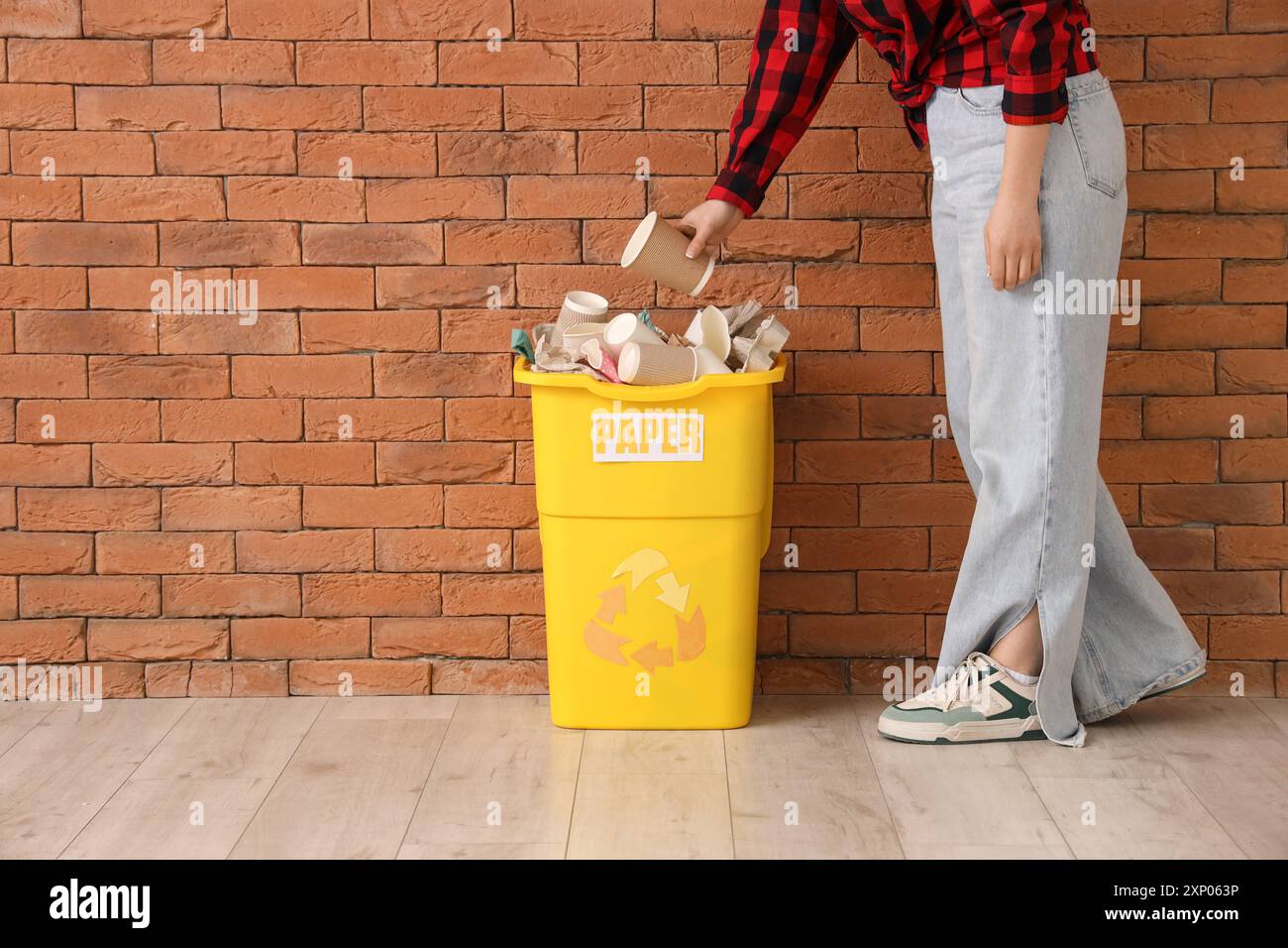 Woman putting garbage into full trash bin with PAPER sign near brick ...