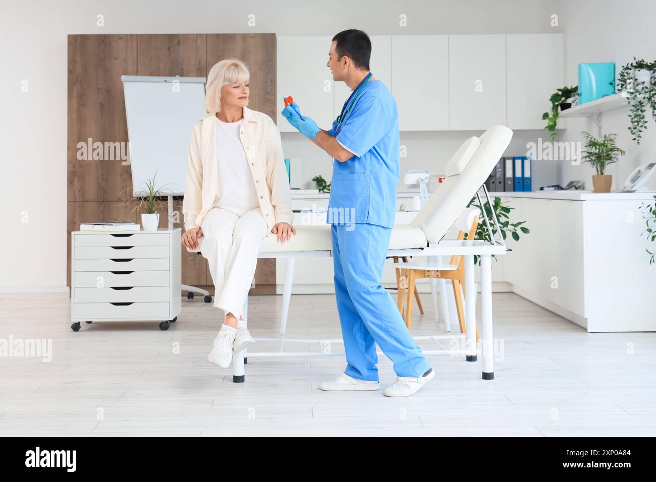 Male endocrinologist showing thyroid gland model to female patient in ...