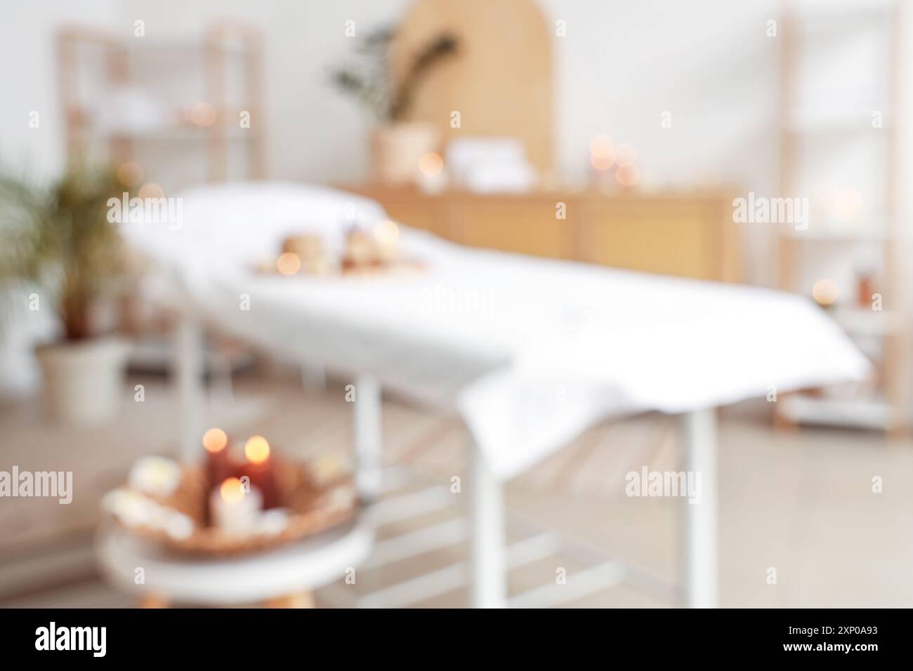 Blurred view of light spa salon with massage couch, burning candles and ...