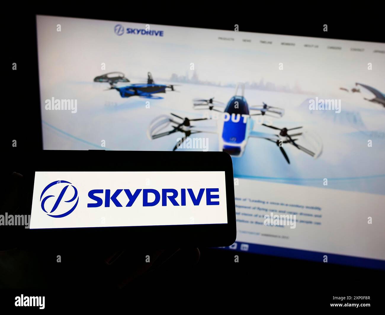 Person holding cellphone with logo of Japanese aviation company SkyDrive Inc. on screen in front ...