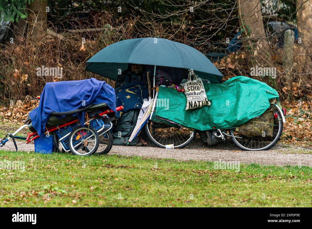 Homeless man in camp on park bench under umbrella with blanket and ...