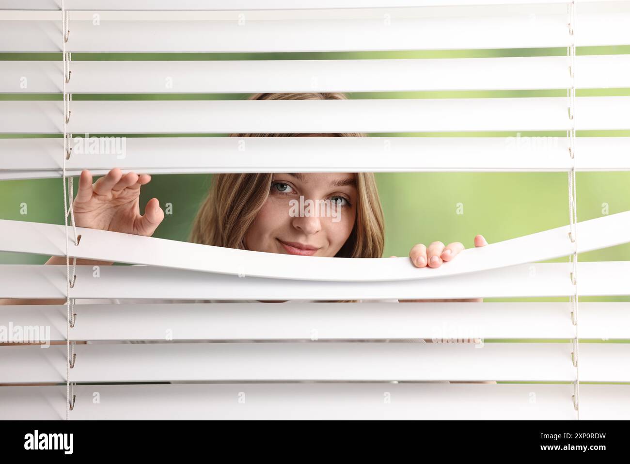 Young woman looking through window blinds on blurred background Stock ...