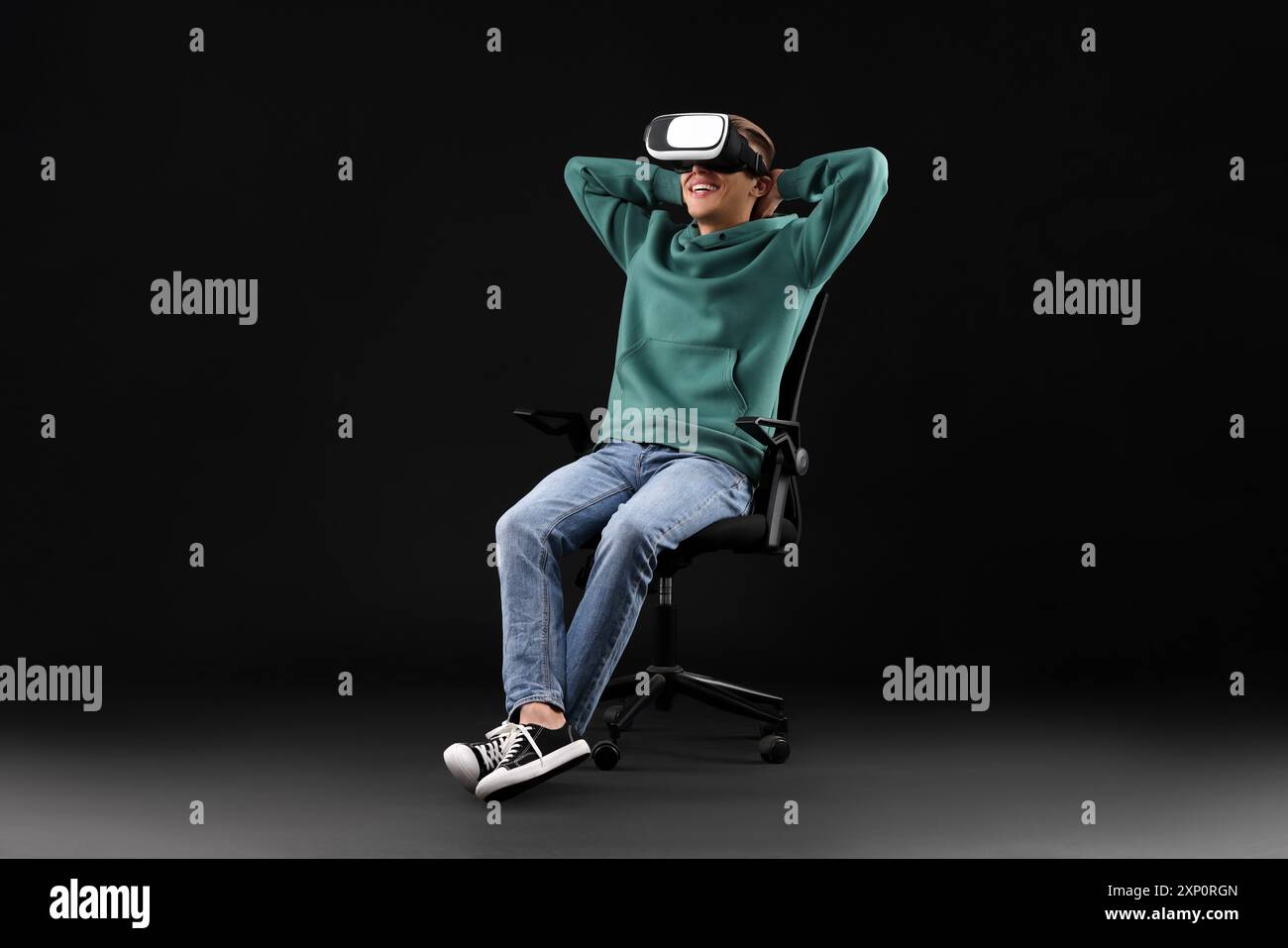 Happy young man with virtual reality headset sitting on chair against ...