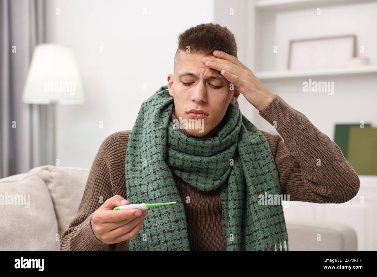 Cold symptom. Young man checking temperature with thermometer at home ...