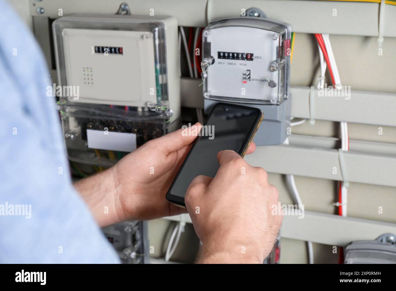 Technician worker with smartphone inspecting electricity meter, closeup ...