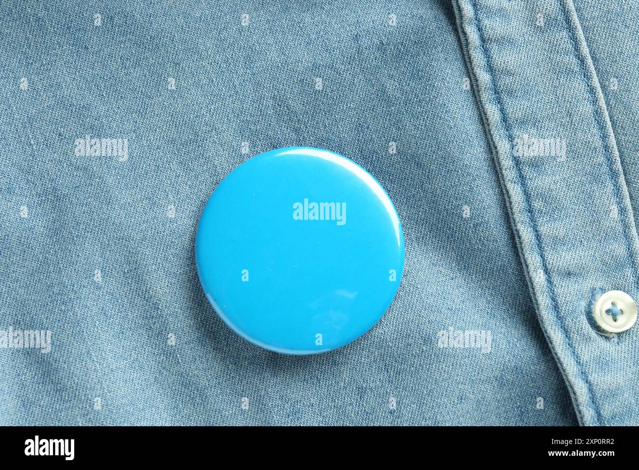Blue button badge pinned on denim shirt, top view. Mockup for design ...