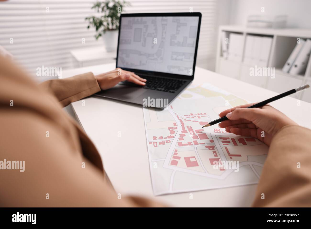 Cartographer working with cadastral map on laptop at white table in ...