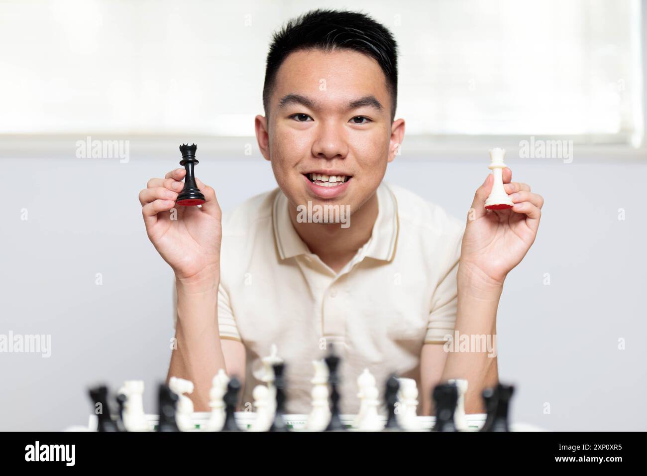 A young Asian teen boy is holding up two chess pieces in front of a ...