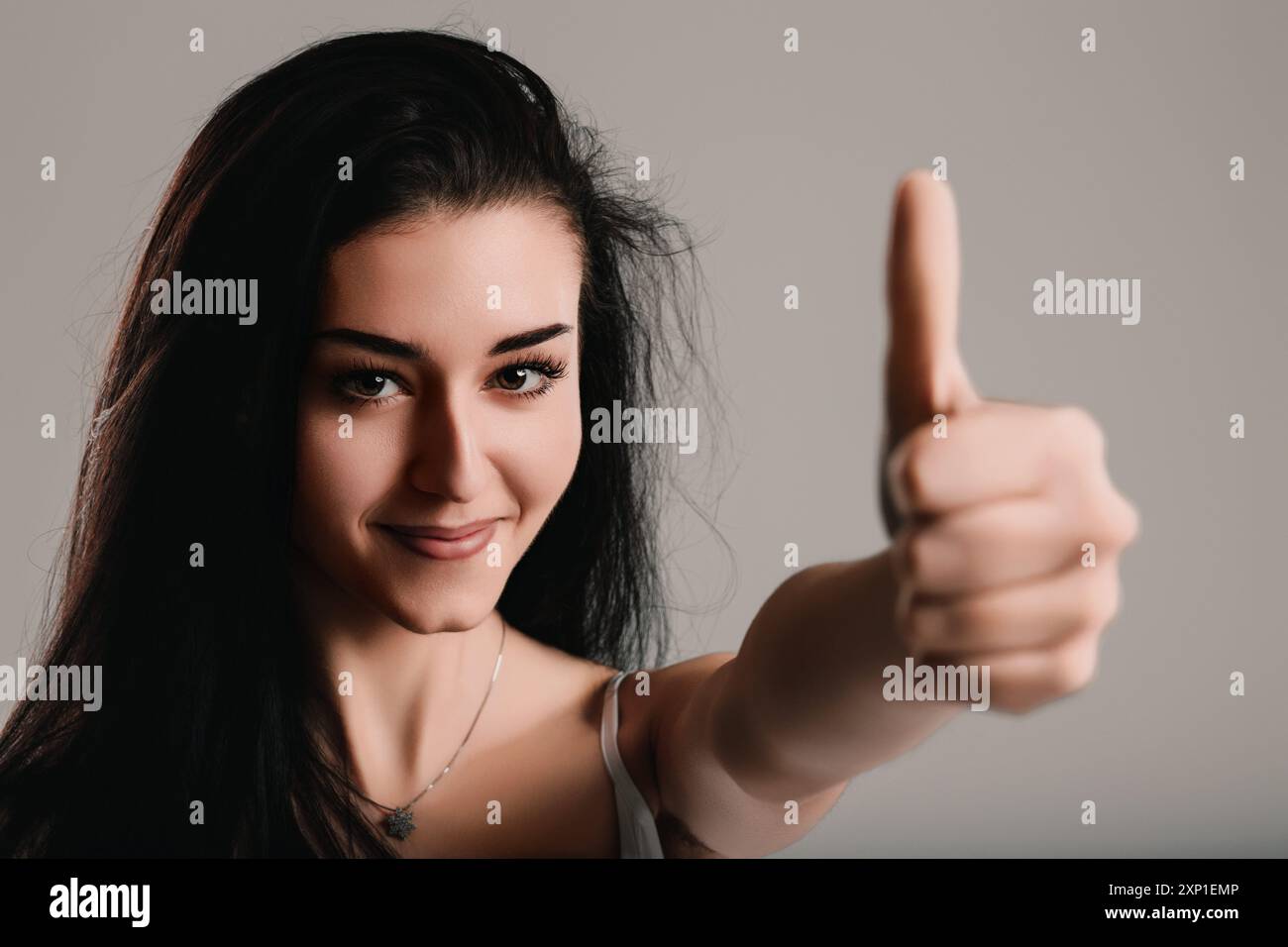 Young woman is showing a thumbs up gesture while smiling slightly ...
