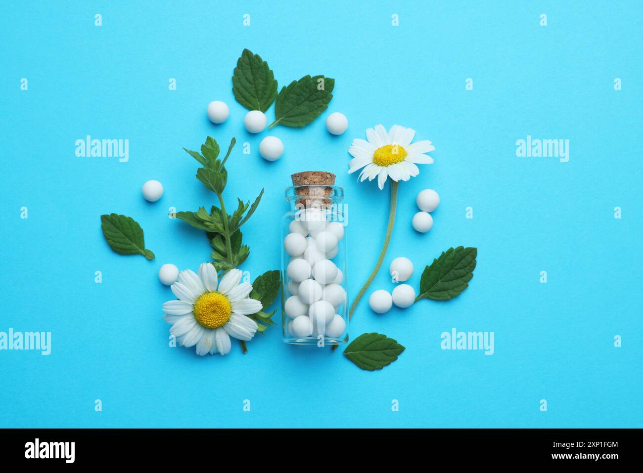 Homeopathy. Glass bottle, pills, chamomiles and green leaves on light ...