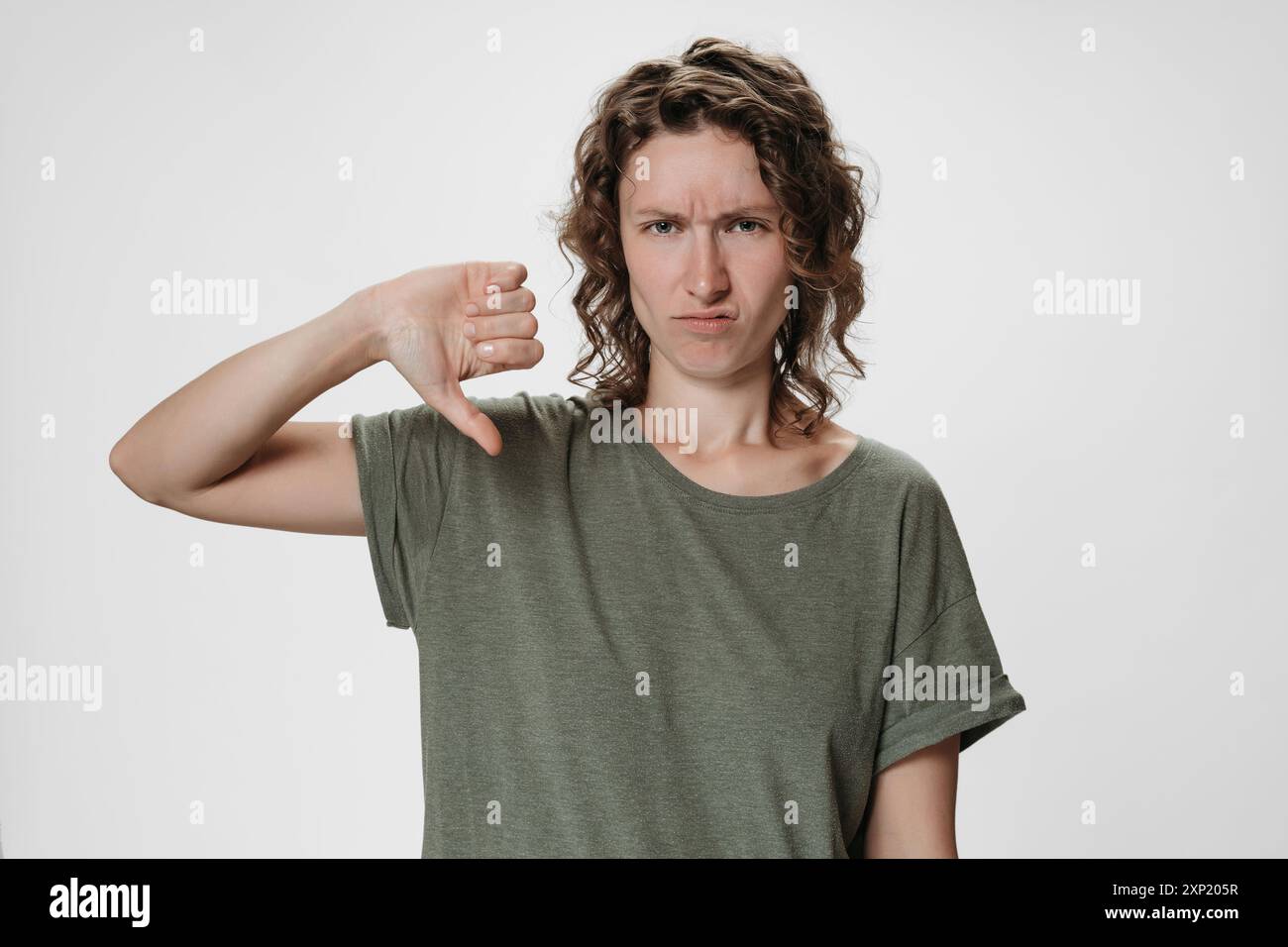 Curly hair woman frowns face, has displeased gives thumb down gesture ...