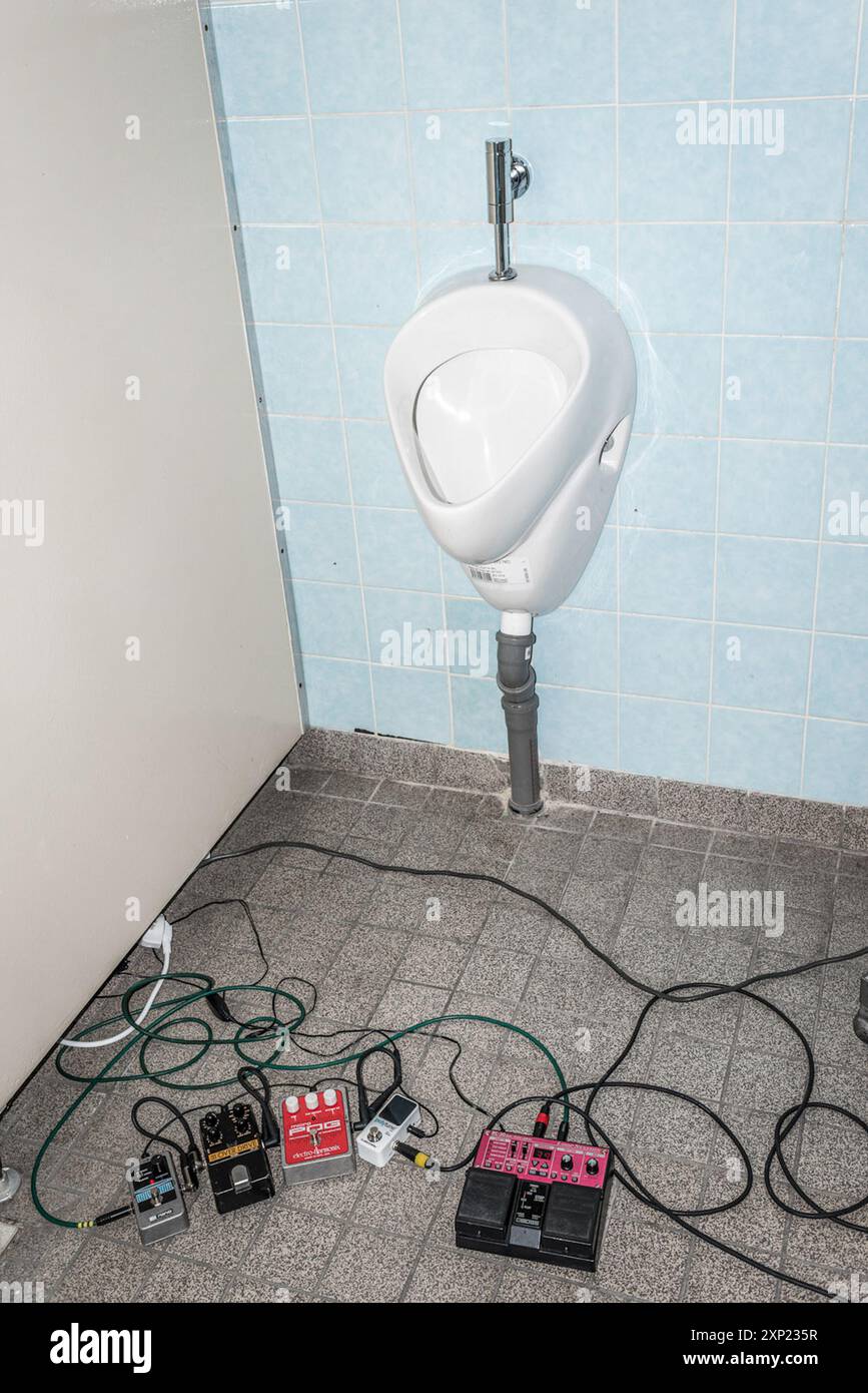Photograph of a urinal next to guitar pedals on the floor, representing ...