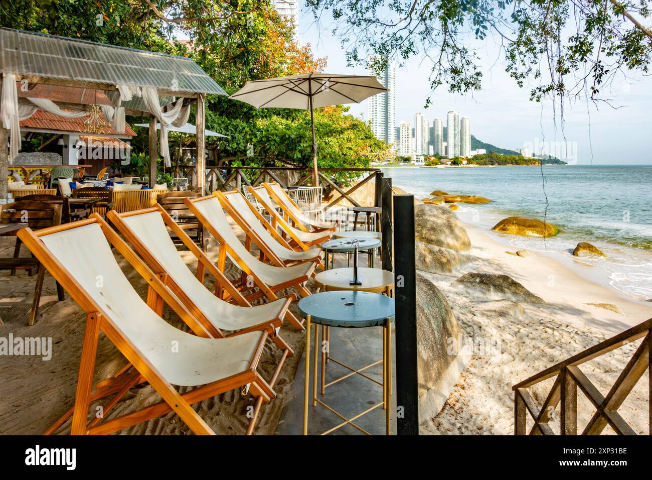 Tables and deck chairs at a beachside bar with views over Tanjing ...