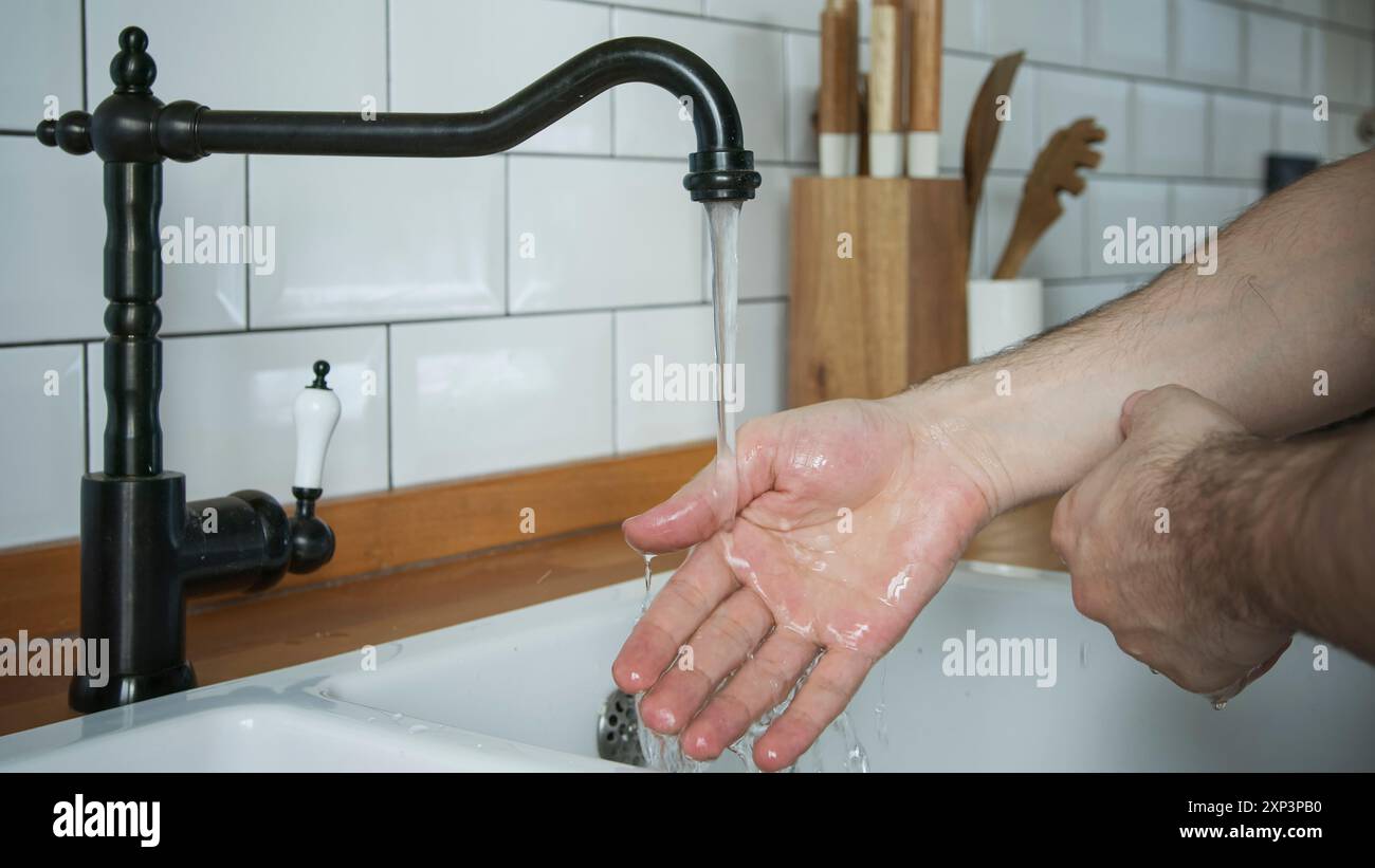 A close-up shot of a person washing hands under a running faucet in a ...
