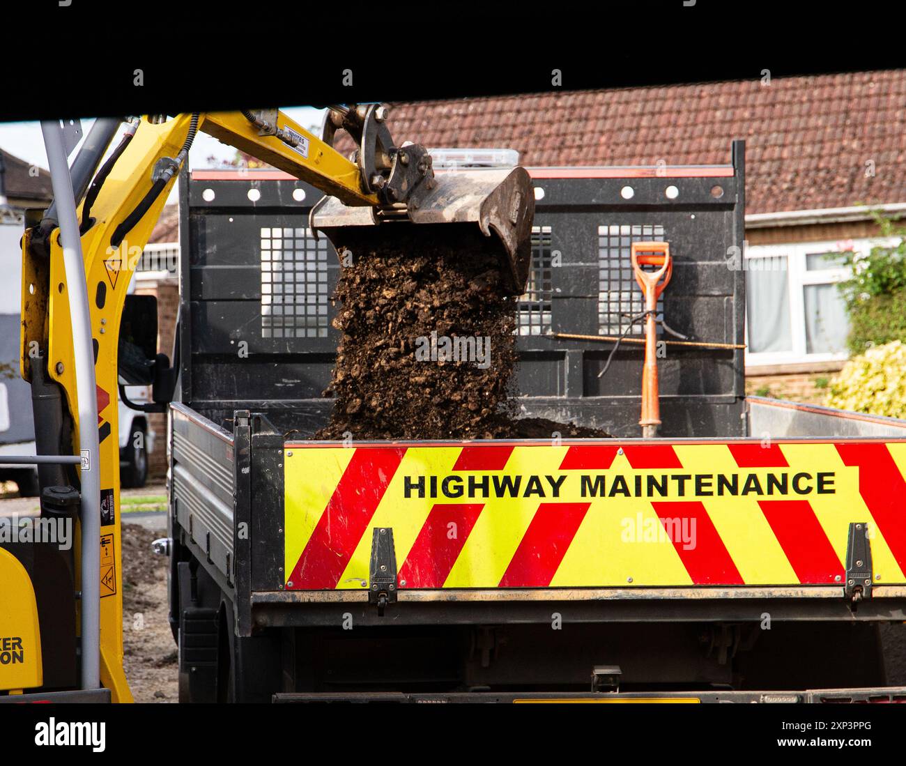 A small excavator emptying soil into a highway maintenance truck with a 'highway maintenance ...