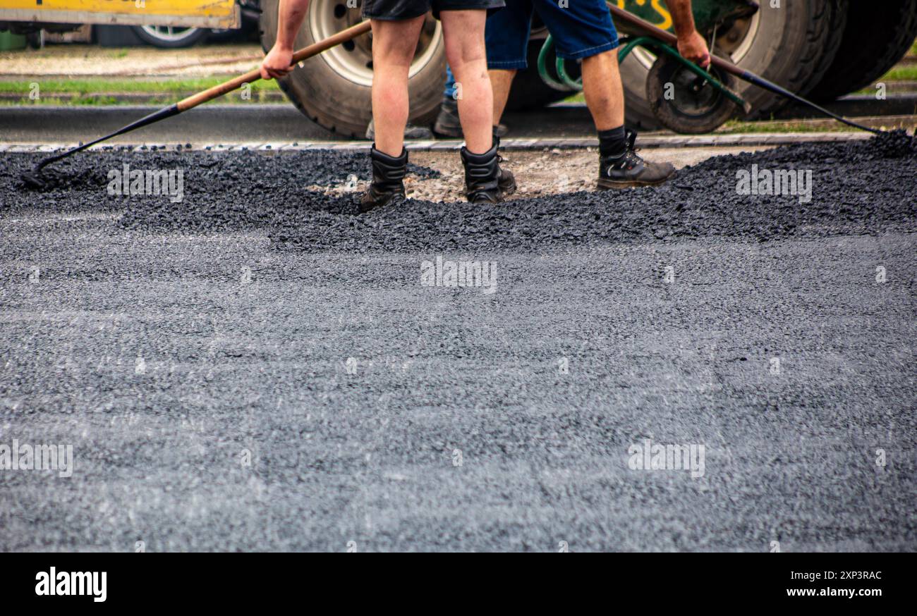 Workers laying fresh asphalt on a road construction site, smoothing out ...