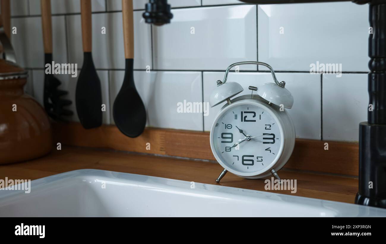 A classic white alarm clock stands on a kitchen counter, with hanging ...