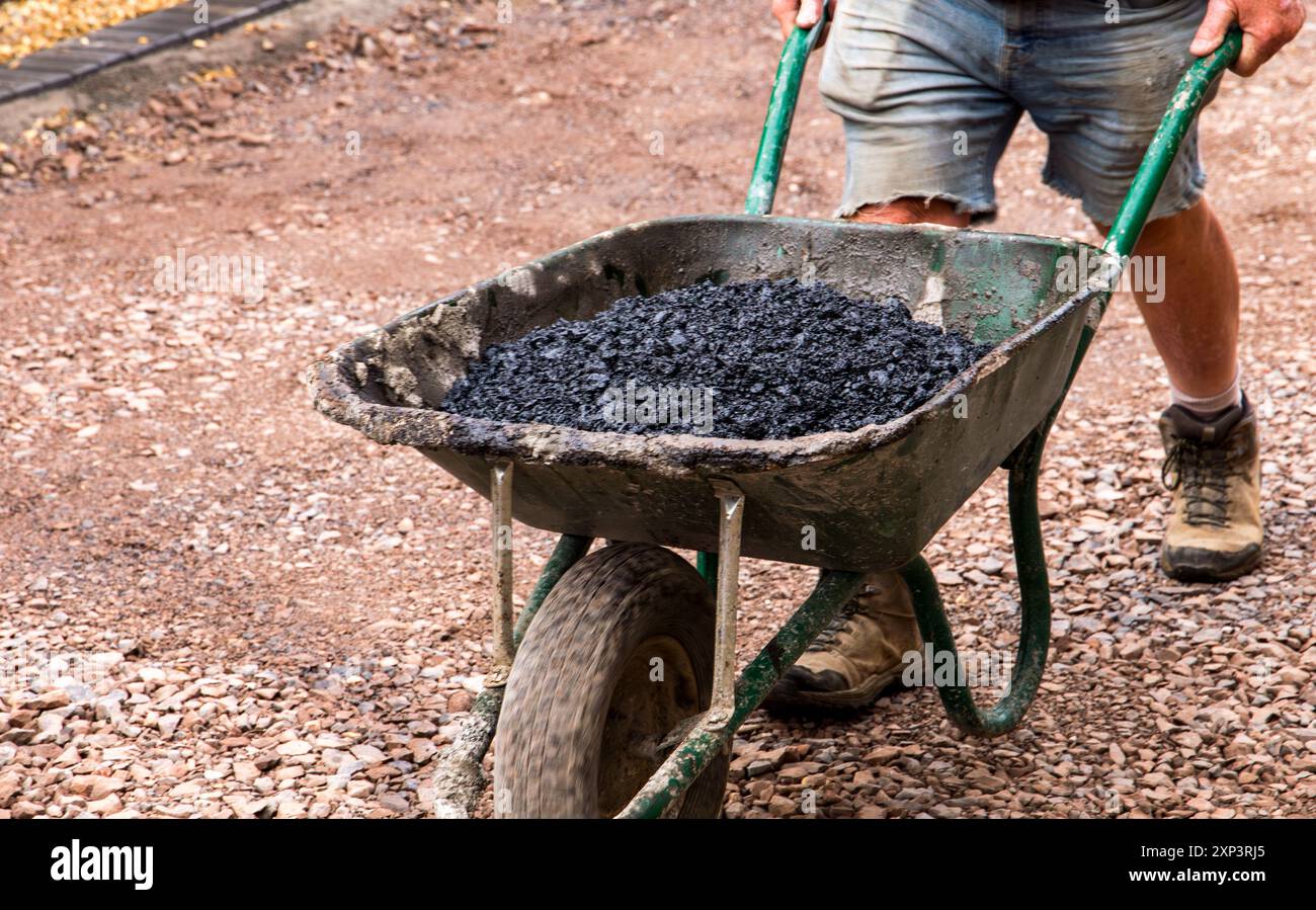 Worker pushing a wheelbarrow filled with asphalt on a construction site ...