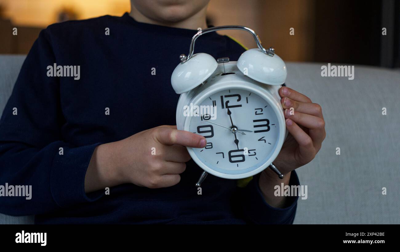 A young boy looking at the camera, holding a vintage alarm clock ...