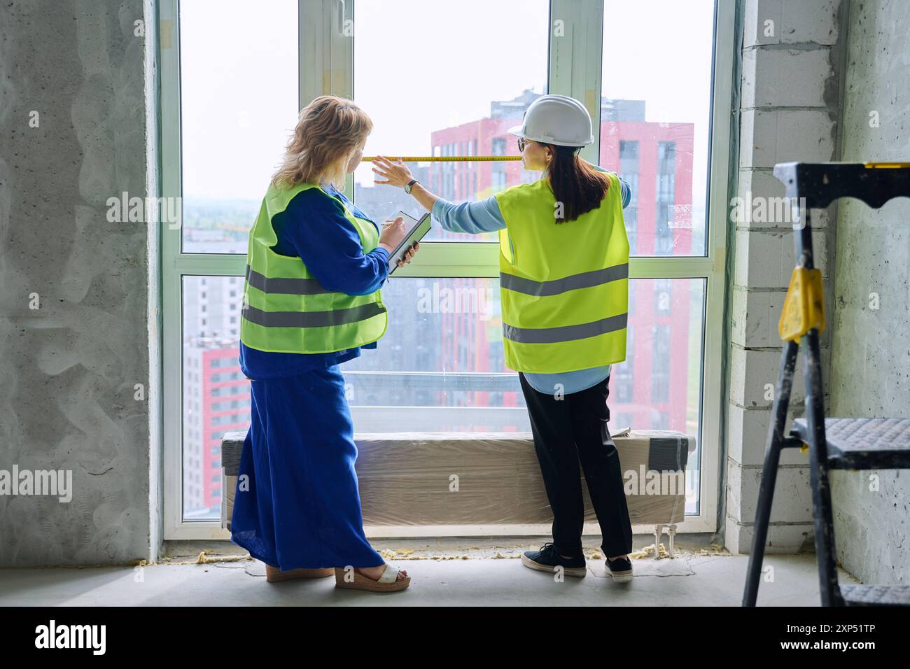 Two female industrial workers taking measurements of windows for ...