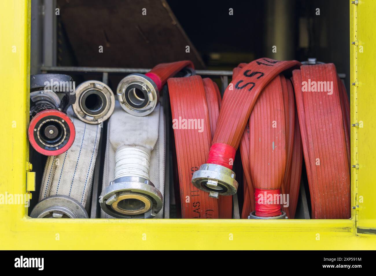 Coiled orange and white fire hoses in yellow compartment ready for ...