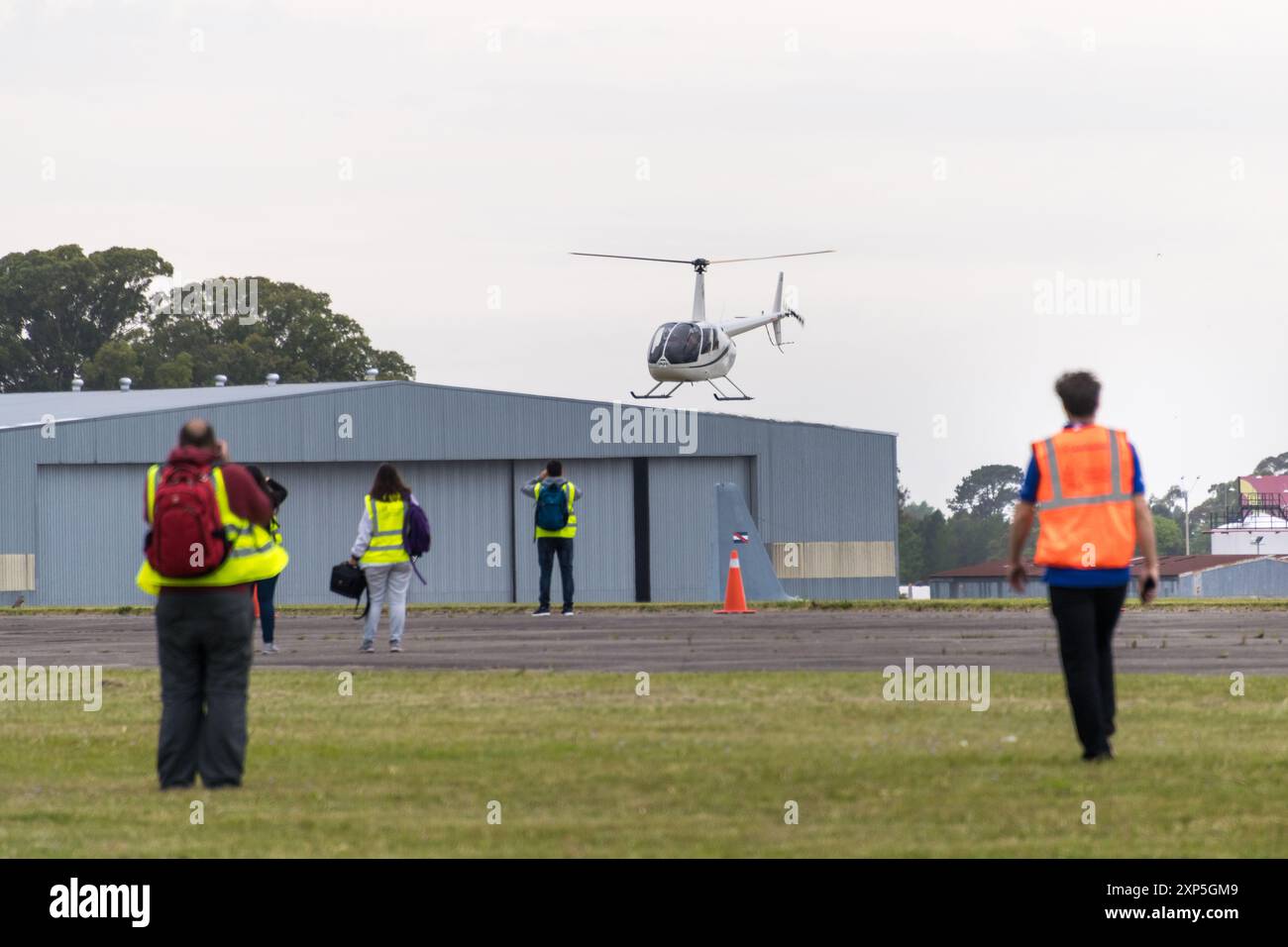 Airfield personnel and passengers observing a helicopter landing at a ...