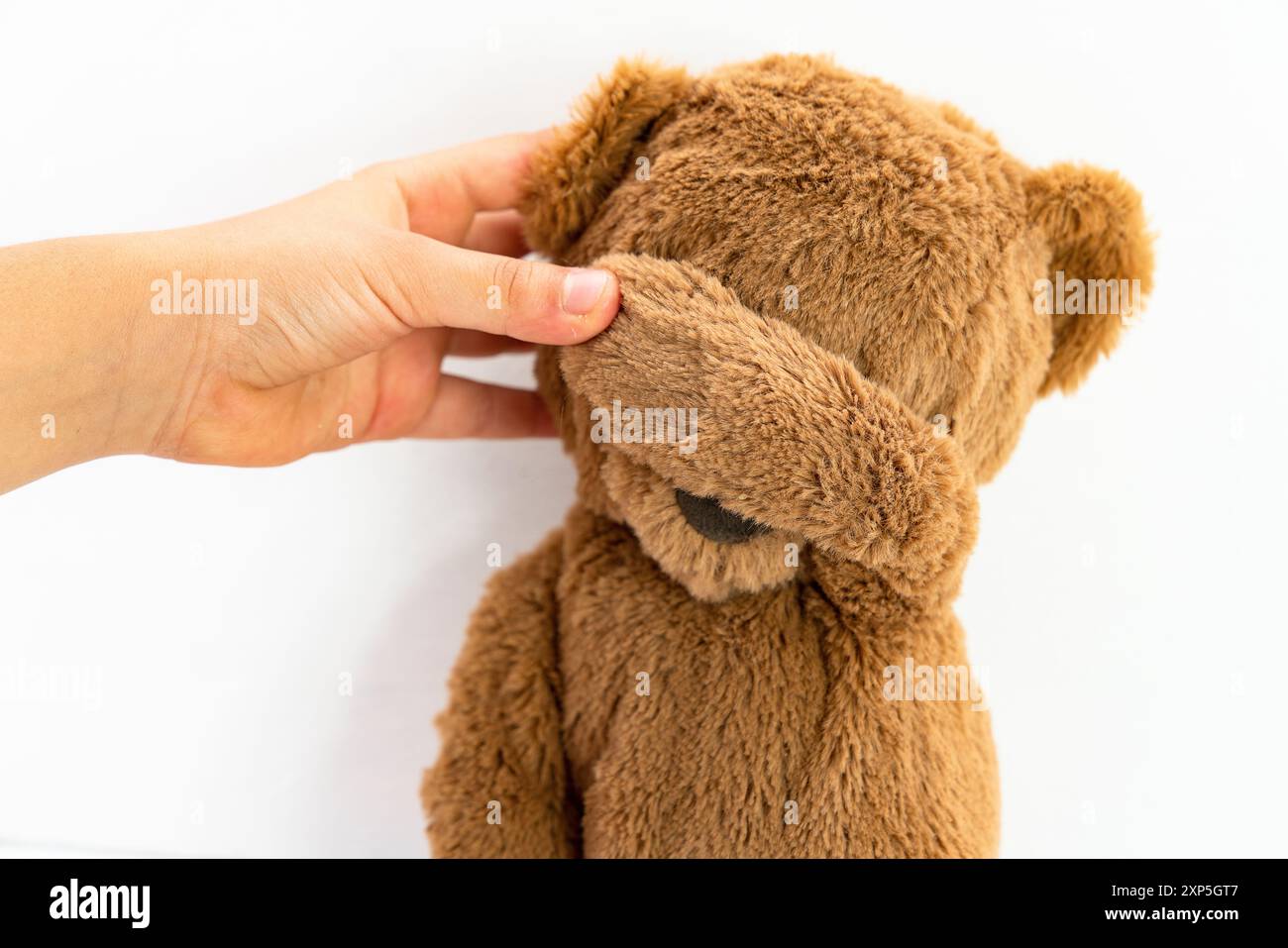 A hand is touching a brown teddy bear's face, with its eyes closed ...