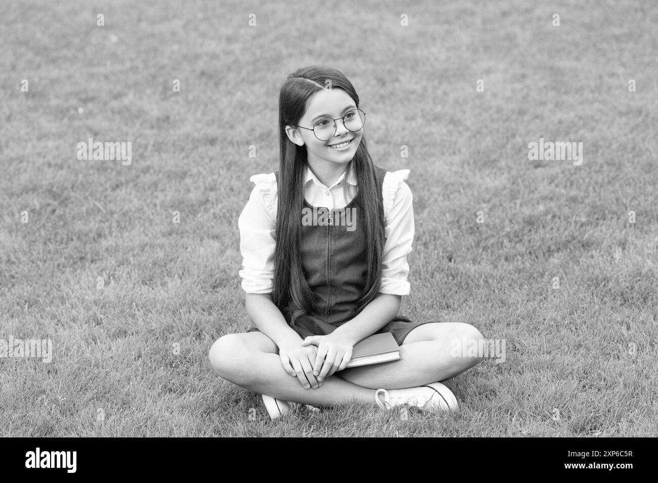 Happy school girl teenager sitting legs crossed on grass. School and education. Back to school ...