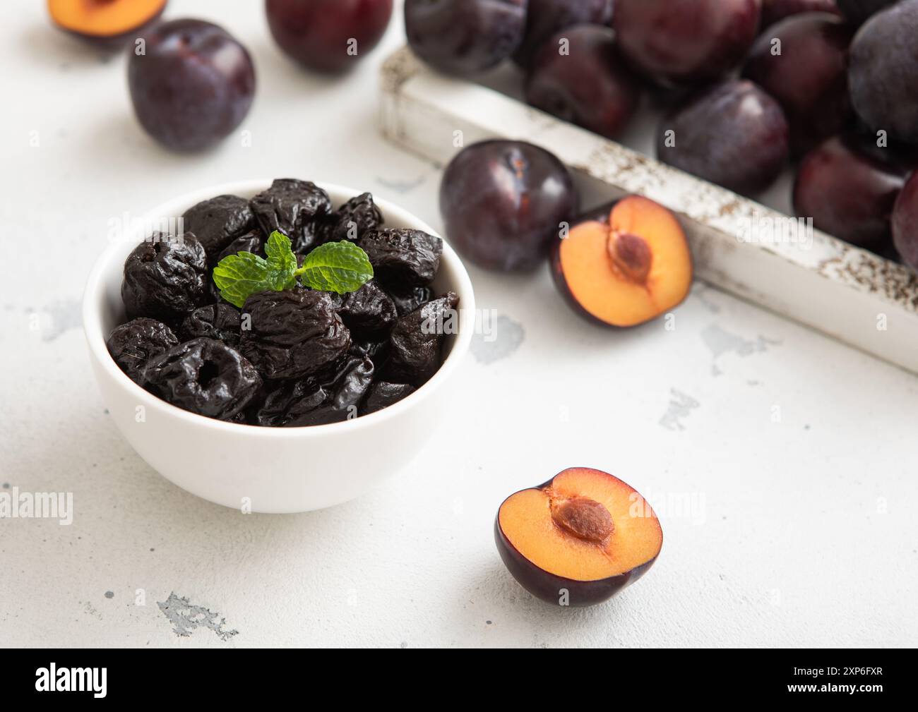 Sweet prunes in glass bowl with ripe plums in wooden box on light ...