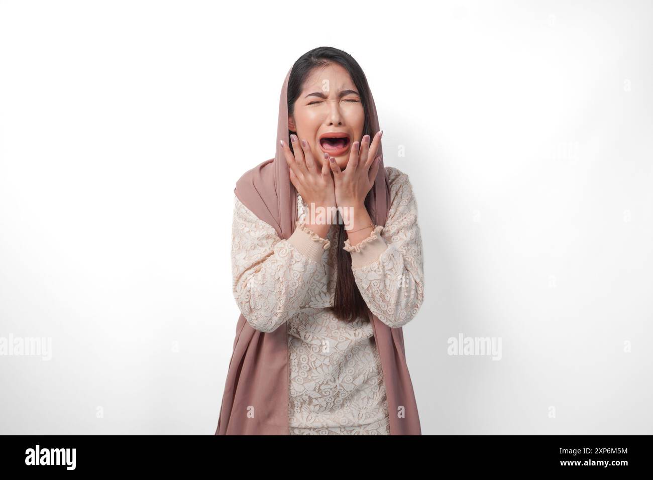 An Asian Muslim woman raising both hands to hold her head feeling ...