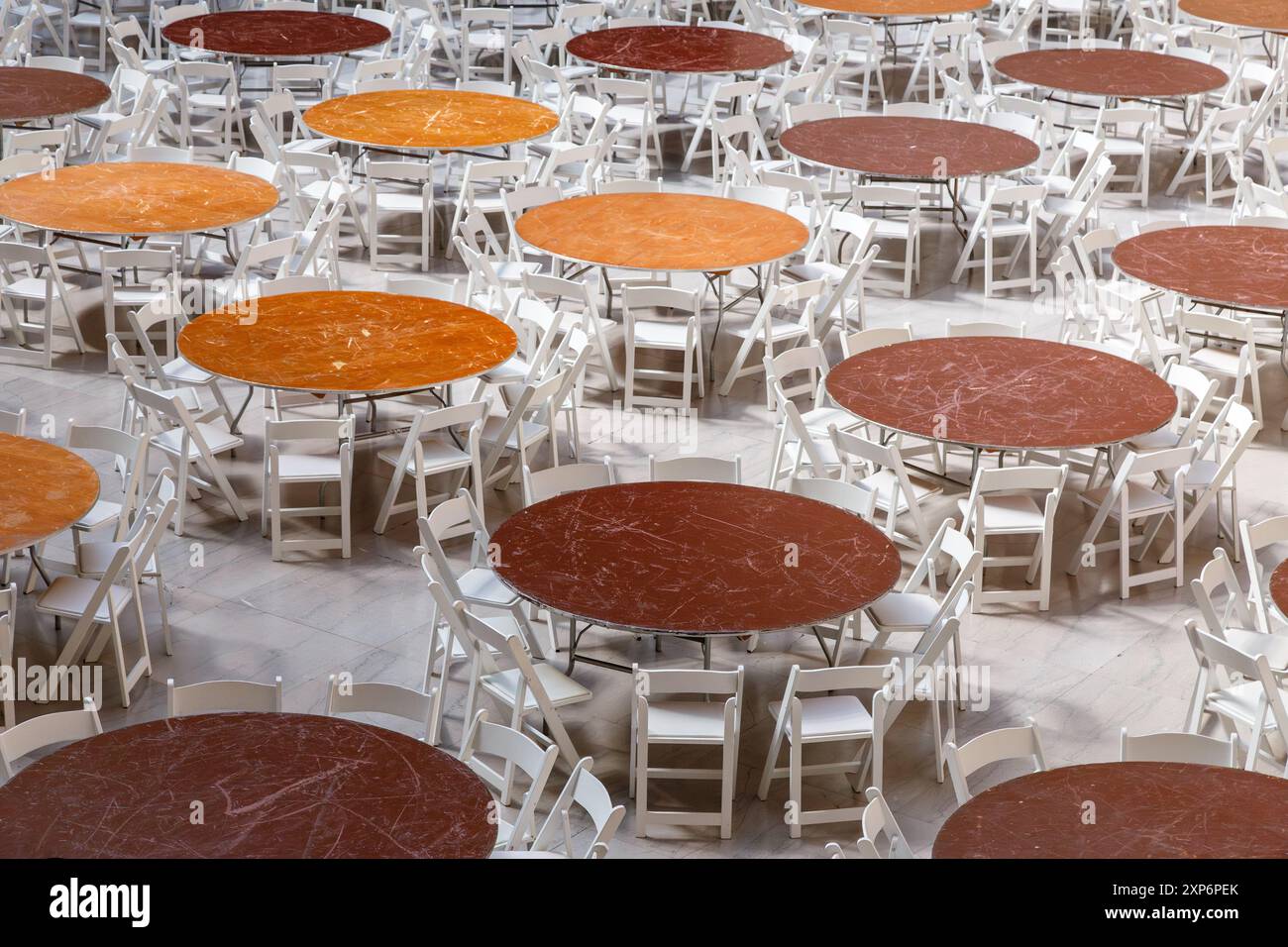 Rows of round dinner tables and chairs stand arranged in a bright hall ...