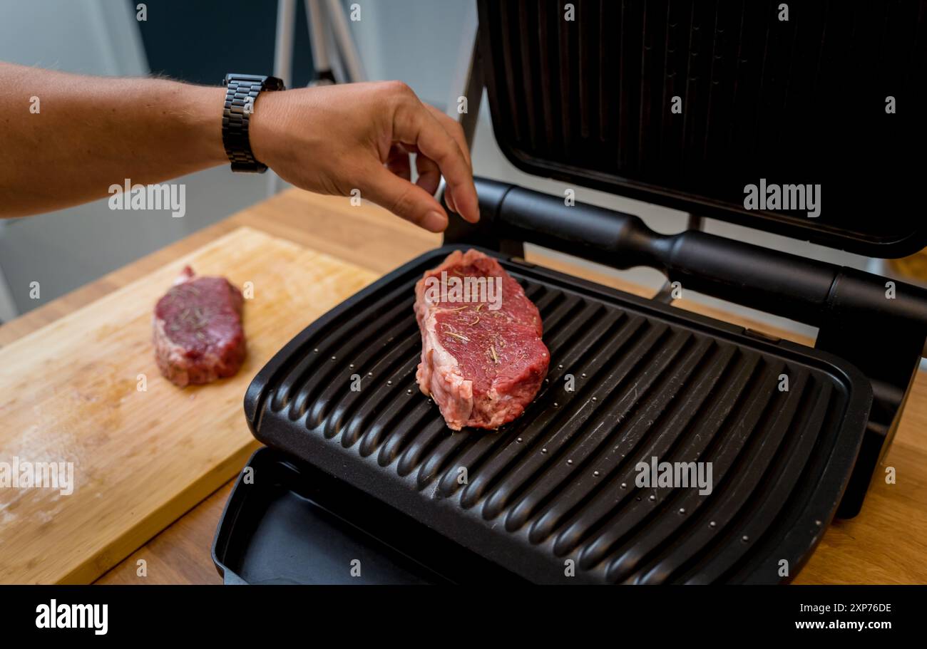 Chef at the kitchen preparing beef steaks on the home electric grill ...
