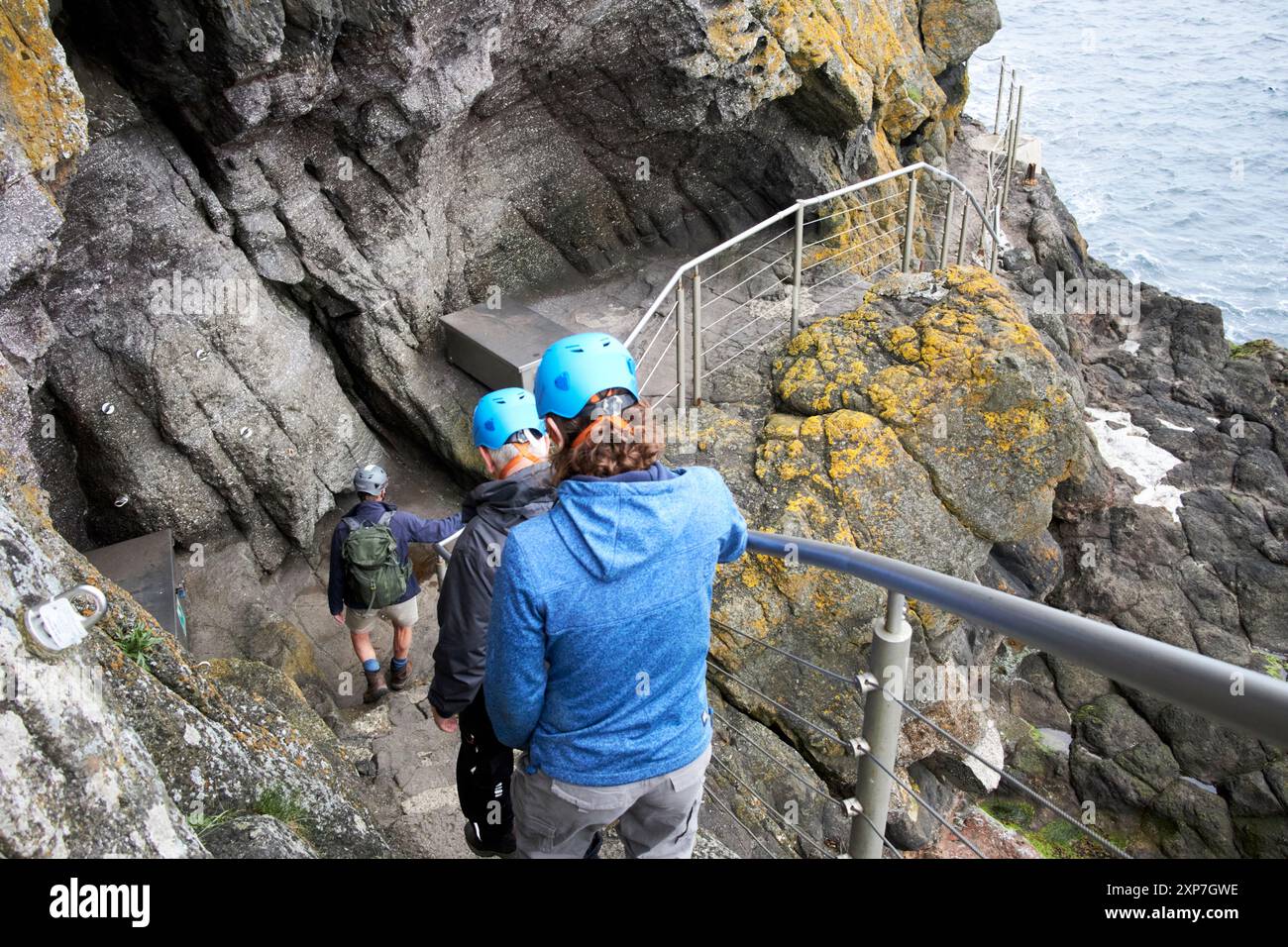tourists wearing helmets follow guide down steep pathway the gobbins ...
