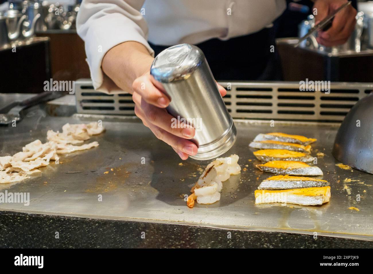 Japanese chef cooking and sprinkling spices on seafood in teppanyaki ...