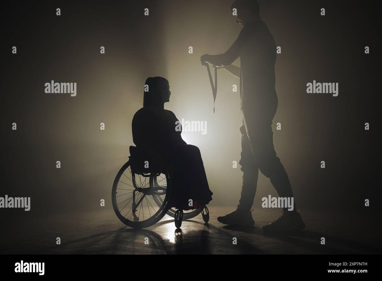Woman in a wheelchair receiving a medal from a man on a dark stage ...