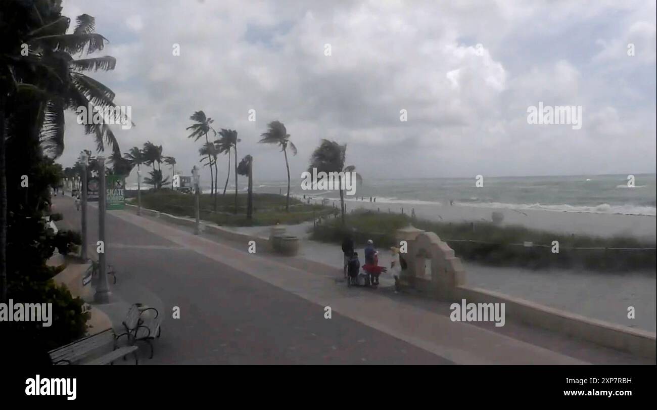 People walk along a windy Hollywood Beach as Tropical Storm Debby moves ...