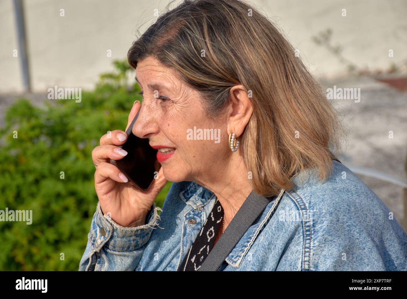 An elderly woman is seated, talking on her mobile phone with a serious ...