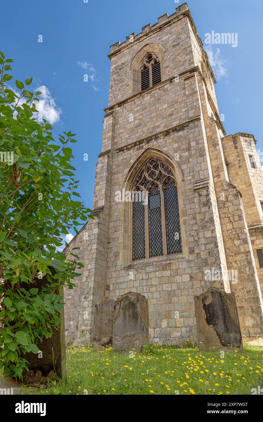 A tower of a medieval church reaches upwards. A tree is one side and a ...