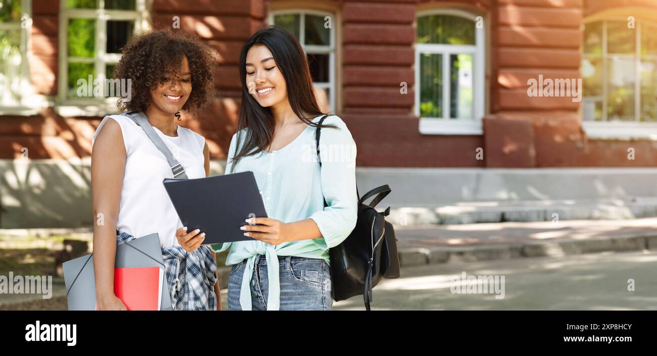 Two multicultural female students standing outdoors near university ...
