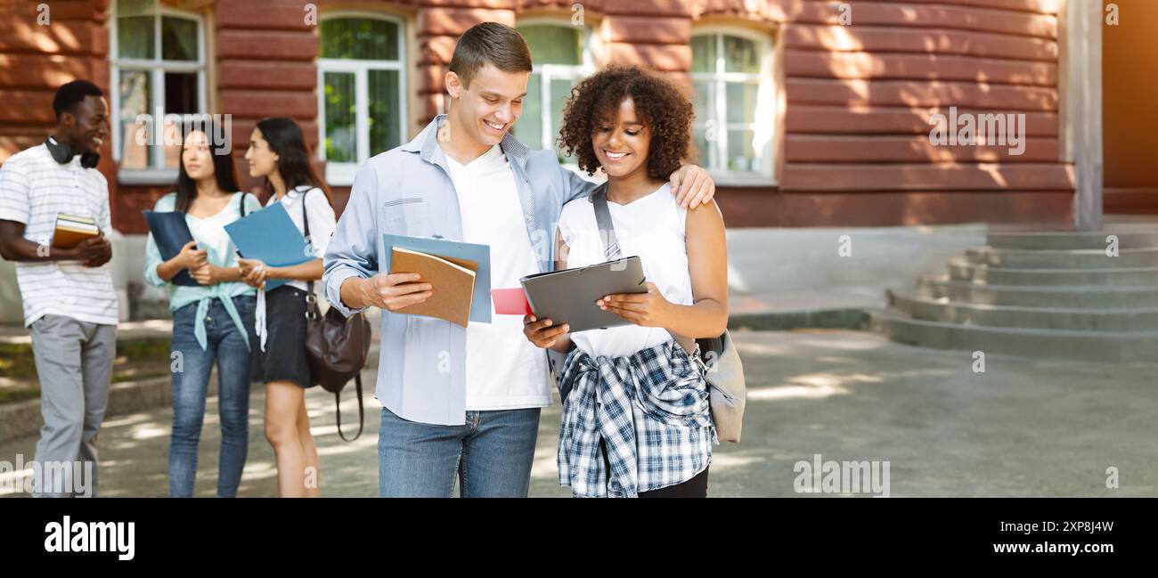 Cheerful student embracing his female classmate outdoors, greeting with ...