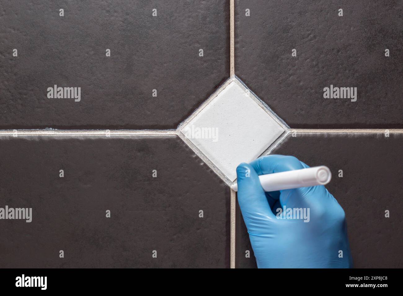Person wearing gloves using grout pen on floor tiles to restore white ...