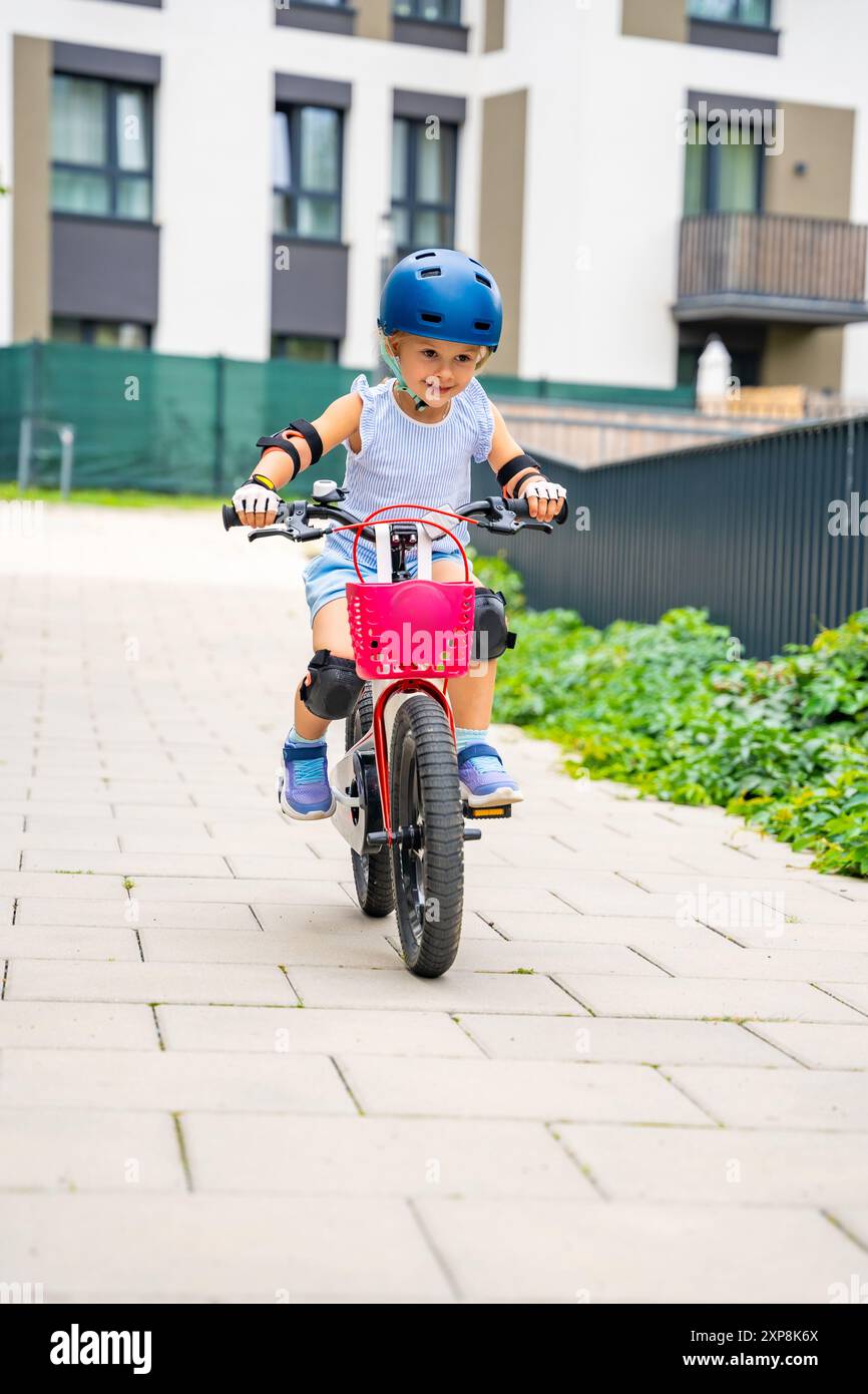 Little girl rides a two-wheeled bicycle Ii the courtyard of apartment ...