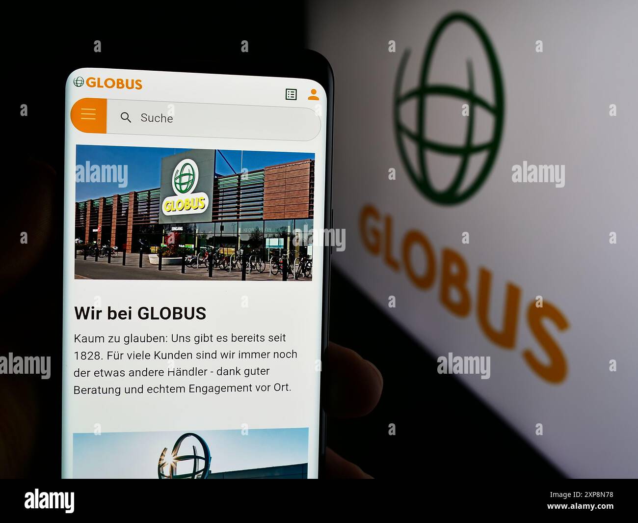 Person holding smartphone with web page of German retail company Globus ...
