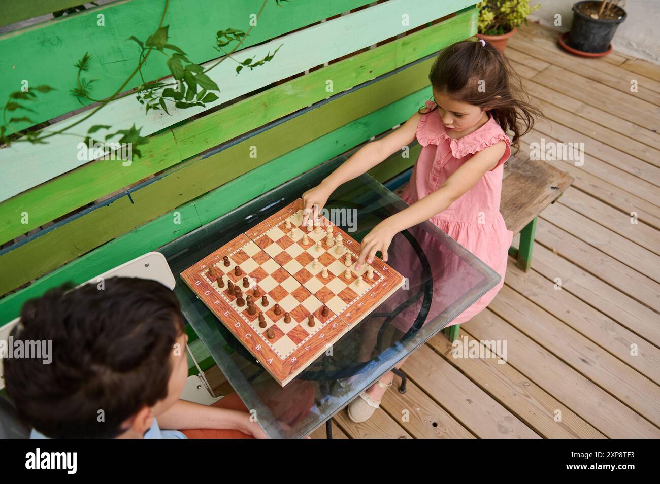 Two children enjoy a game of chess on a wooden patio, focusing on ...