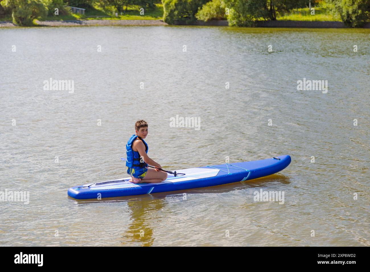 A young guy sitting down rides a SUP board, overcoming the waves with ...