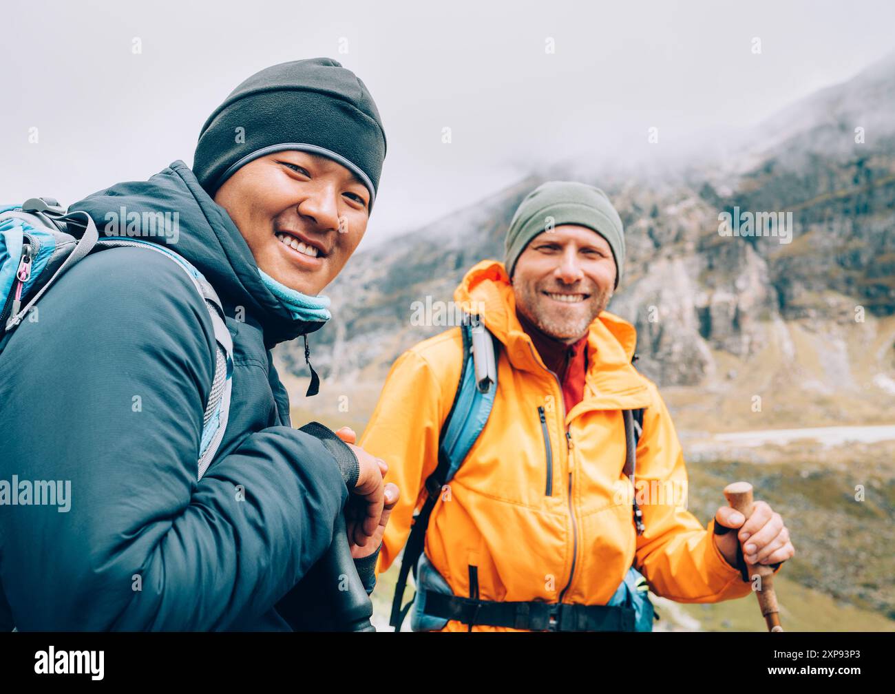 Caucasian and Sherpa men with backpacks together smiling at camera ...